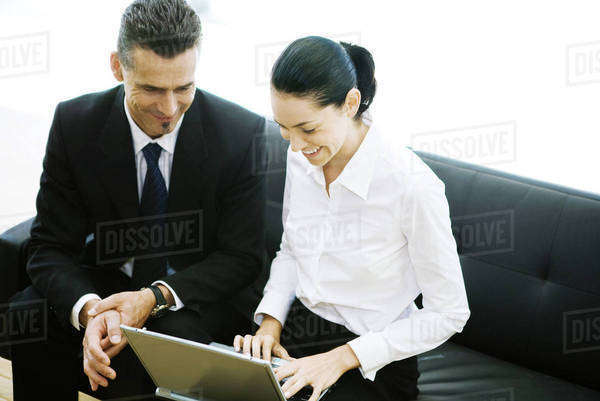 Male and female business associates sitting in lobby, using laptop ...