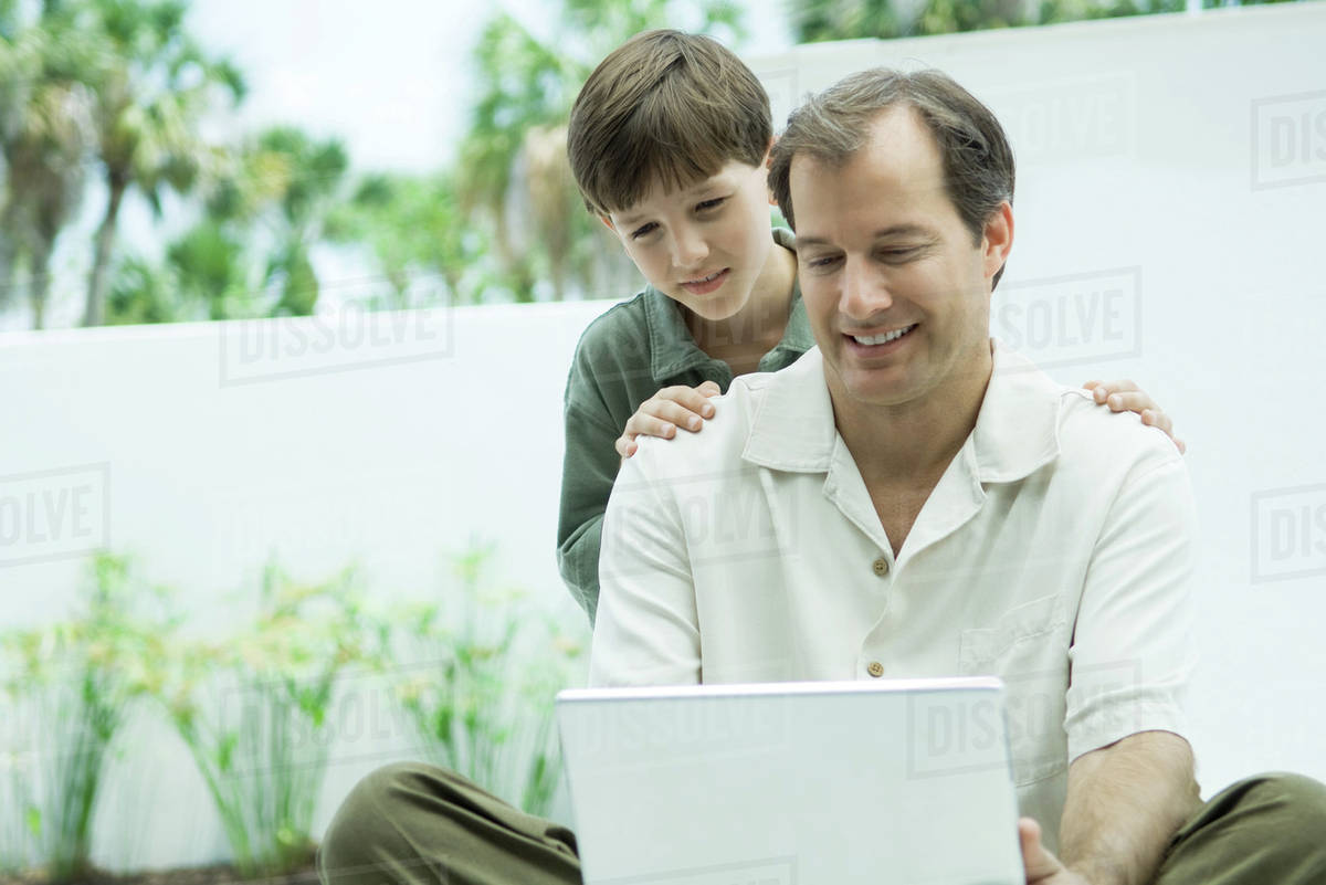 Man using laptop computer, son looking over his shoulder - Royalty-free ...