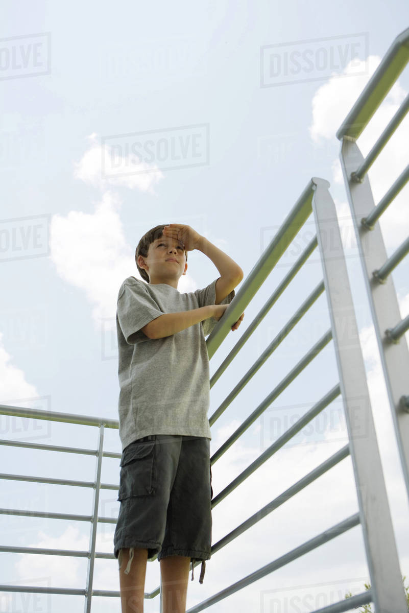 Boy standing on balcony shading eyes, looking at view - Royalty-free ...