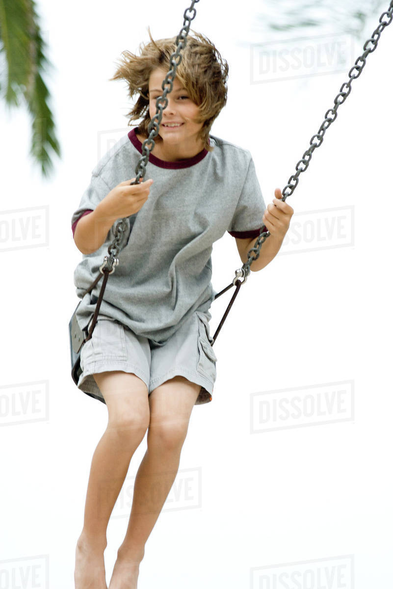 Boy swinging, smiling at camera, full length - Stock Photo - Dissolve