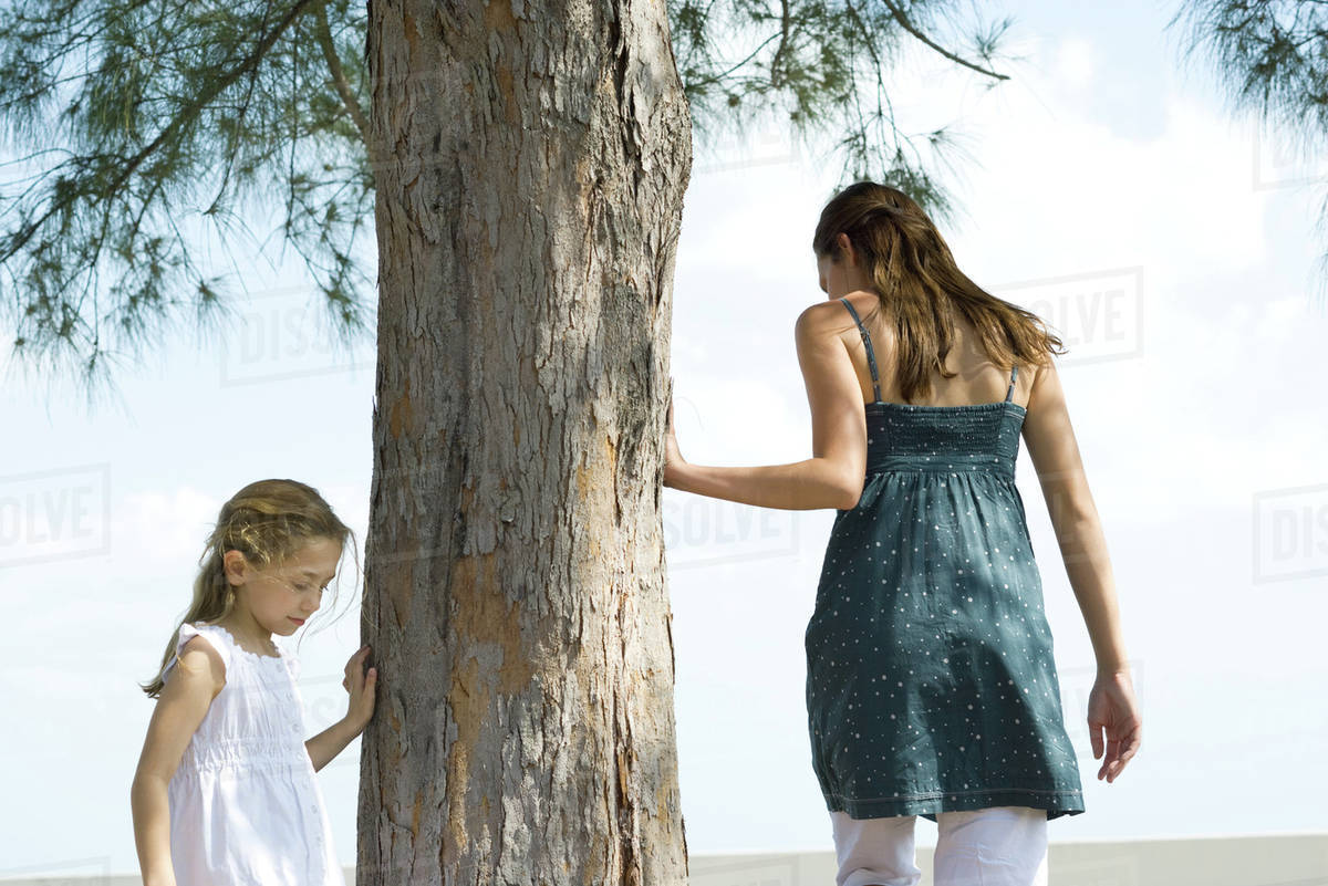 Two sisters walking around tree, touching trunk, low angle view ...