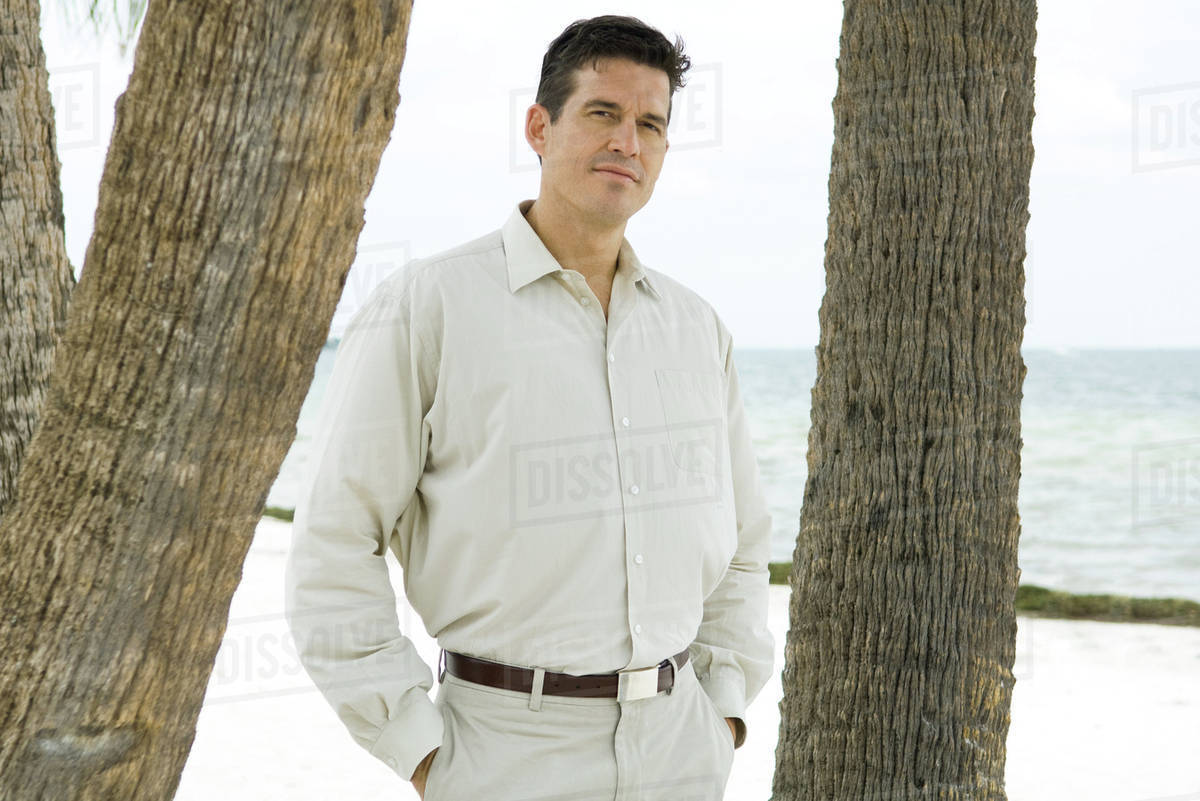 Man standing between tree trunks, hands in pockets, looking at camera ...