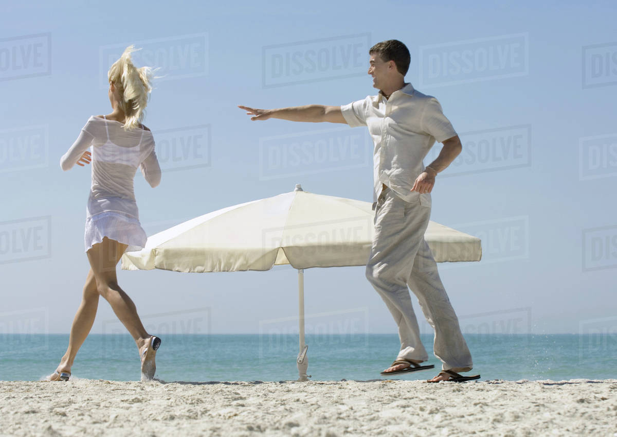 Couple chasing each other around parasol on beach - Royalty-free Stock ...