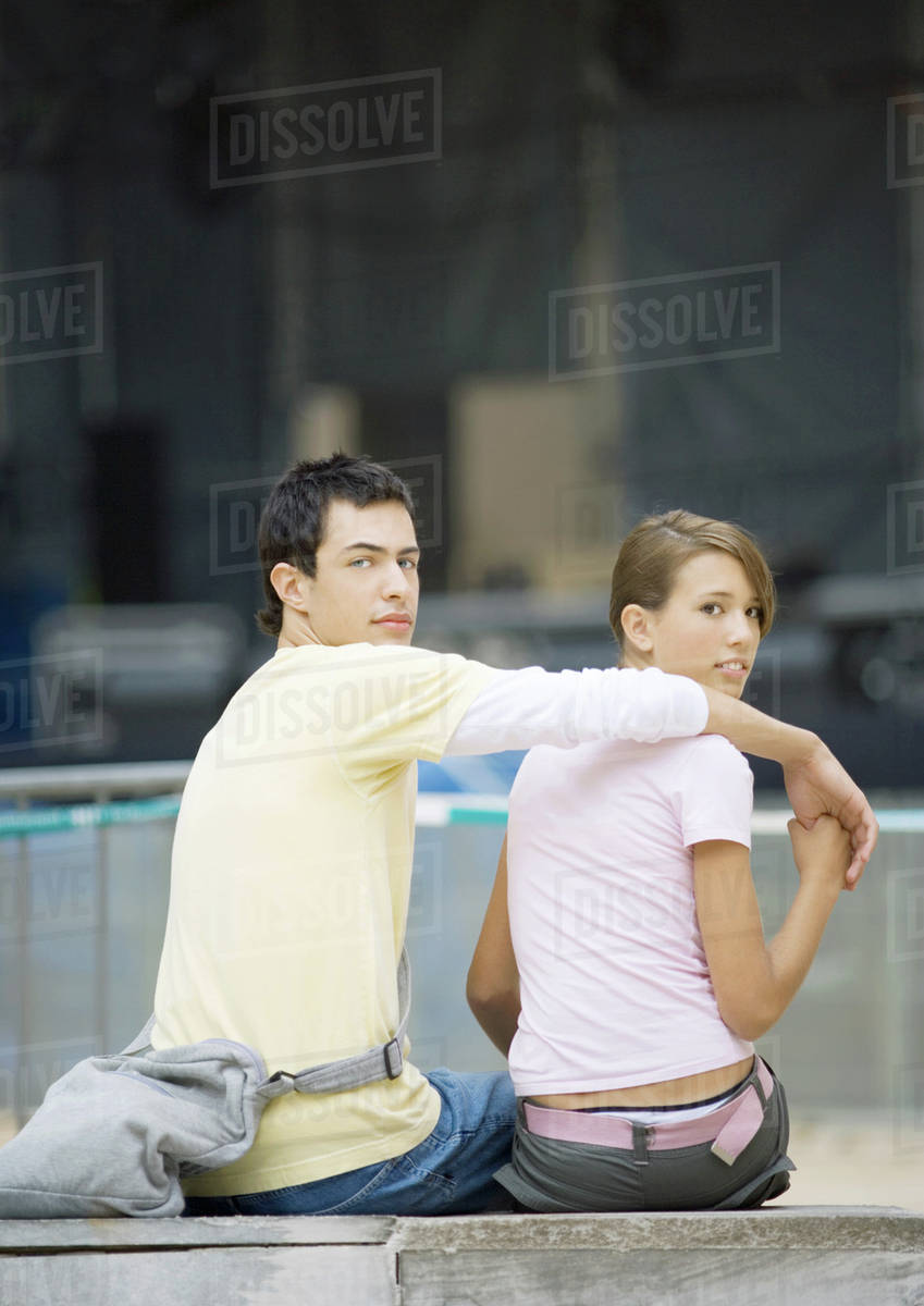 Teen couple sitting, looking over shoulder - Stock Photo - Dissolve
