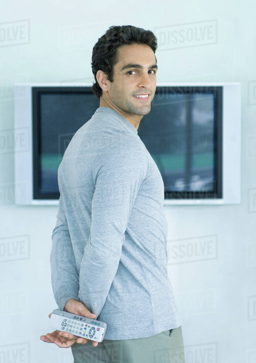 Man standing in front of widescreen TV, holding two remote controls ...