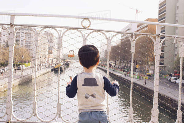 Little boy standing on bridge looking over canal - Stock Photo - Dissolve
