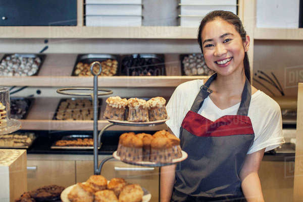Woman smiling behind bakery counter, portrait - Stock Photo - Dissolve