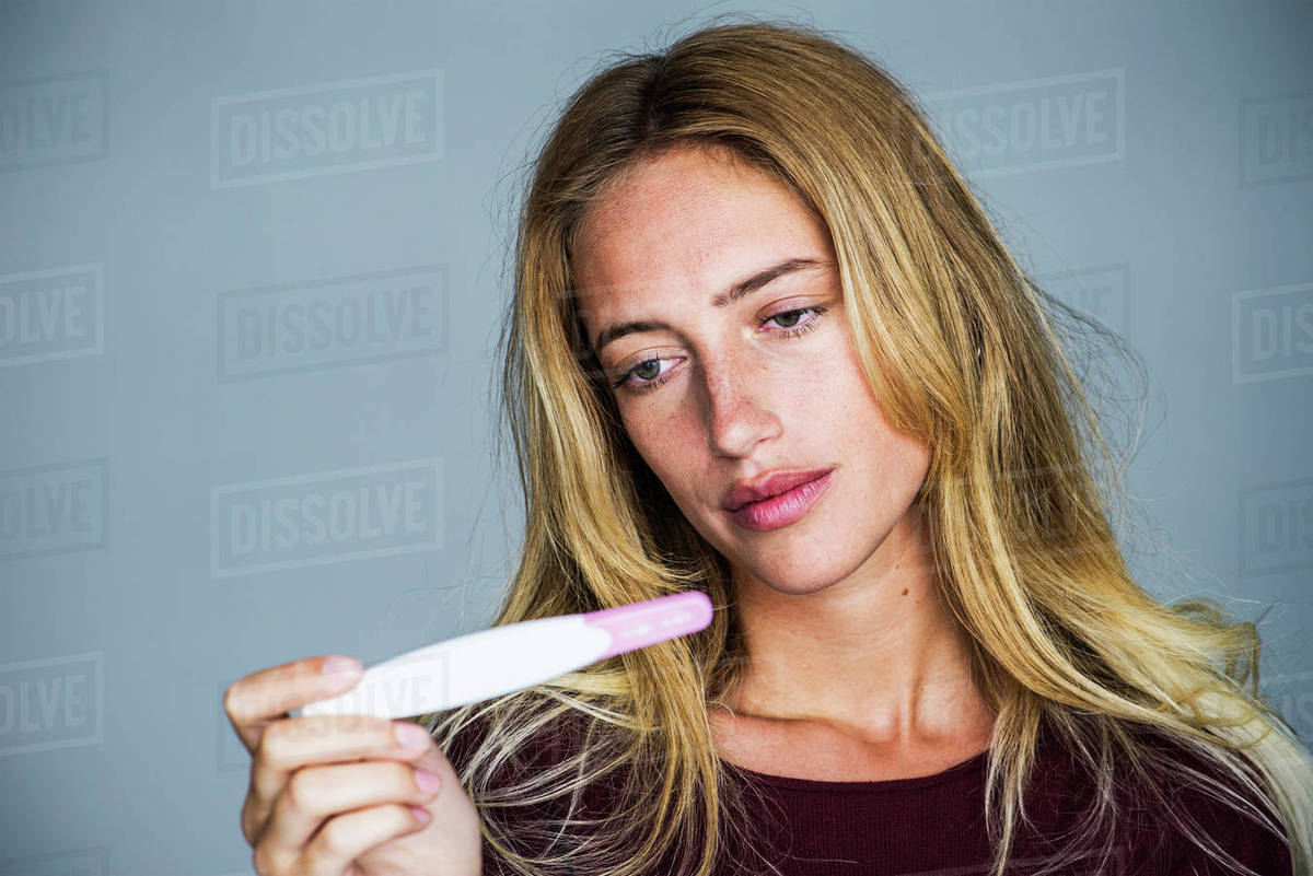 Young woman looking at pregnancy test with disappointed expression ...