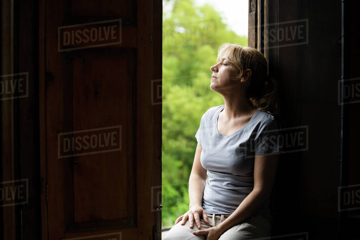 Thoughtful woman sitting on window - Stock Photo - Dissolve