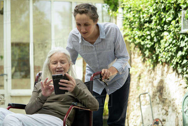Senior female patient showing mobile phone to young home carer ...