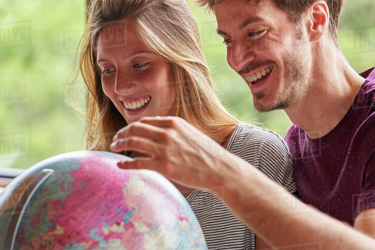 Young couple exploring world globe while sitting in living room ...