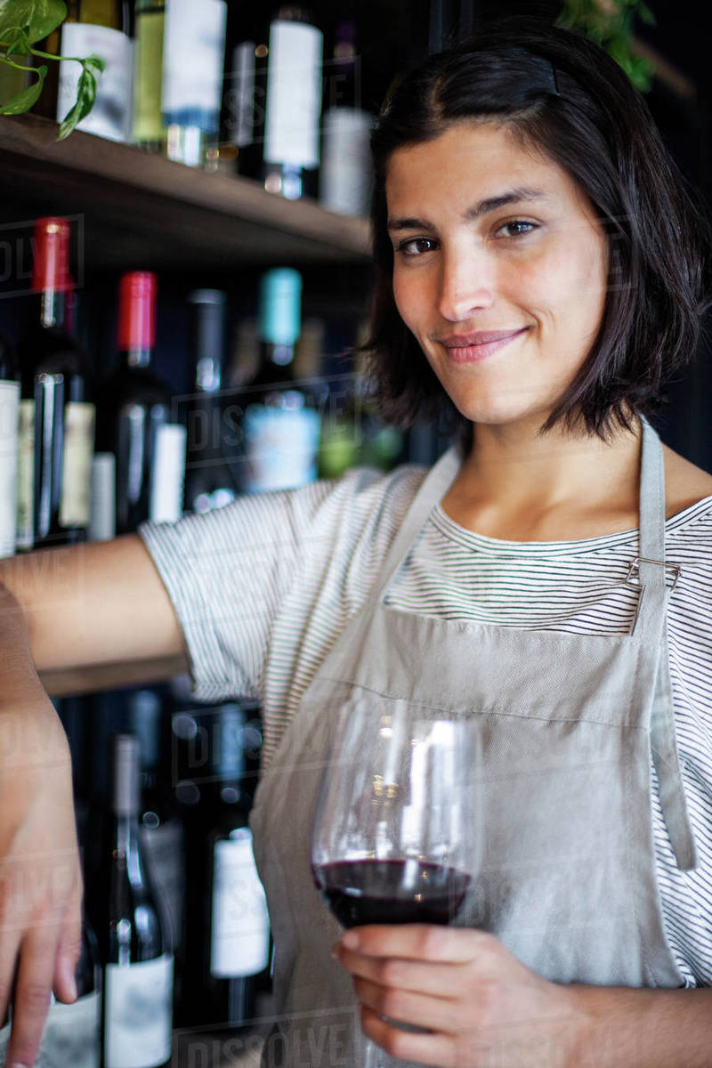 Female sommelier holding glass of wine while standing in liquor store ...