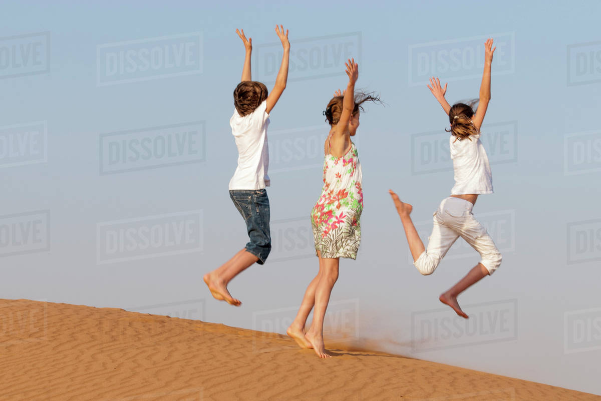 Children jumping on sand, rear view - Royalty-free Stock Photo | Dissolve