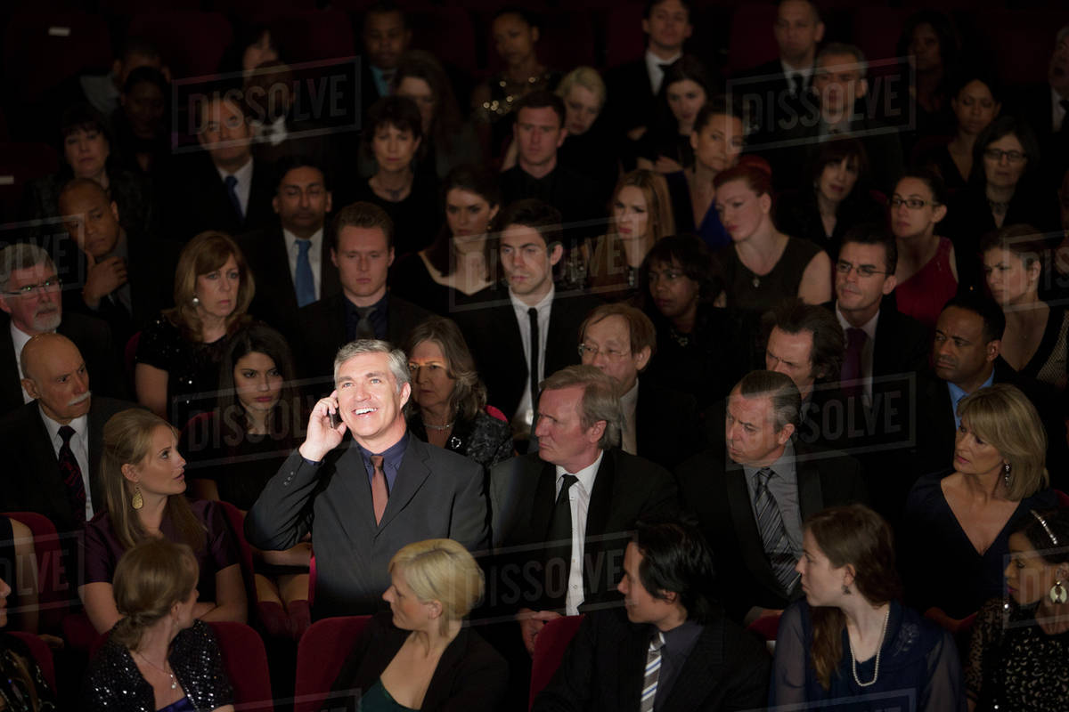 Man talking on cell phone in theater audience - Stock Photo - Dissolve
