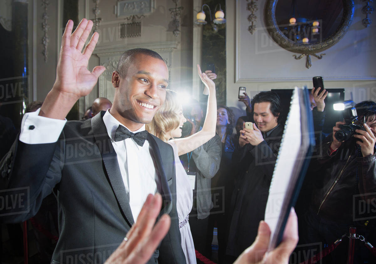 Well dressed male celebrity waving to fans and paparazzi at red carpet ...