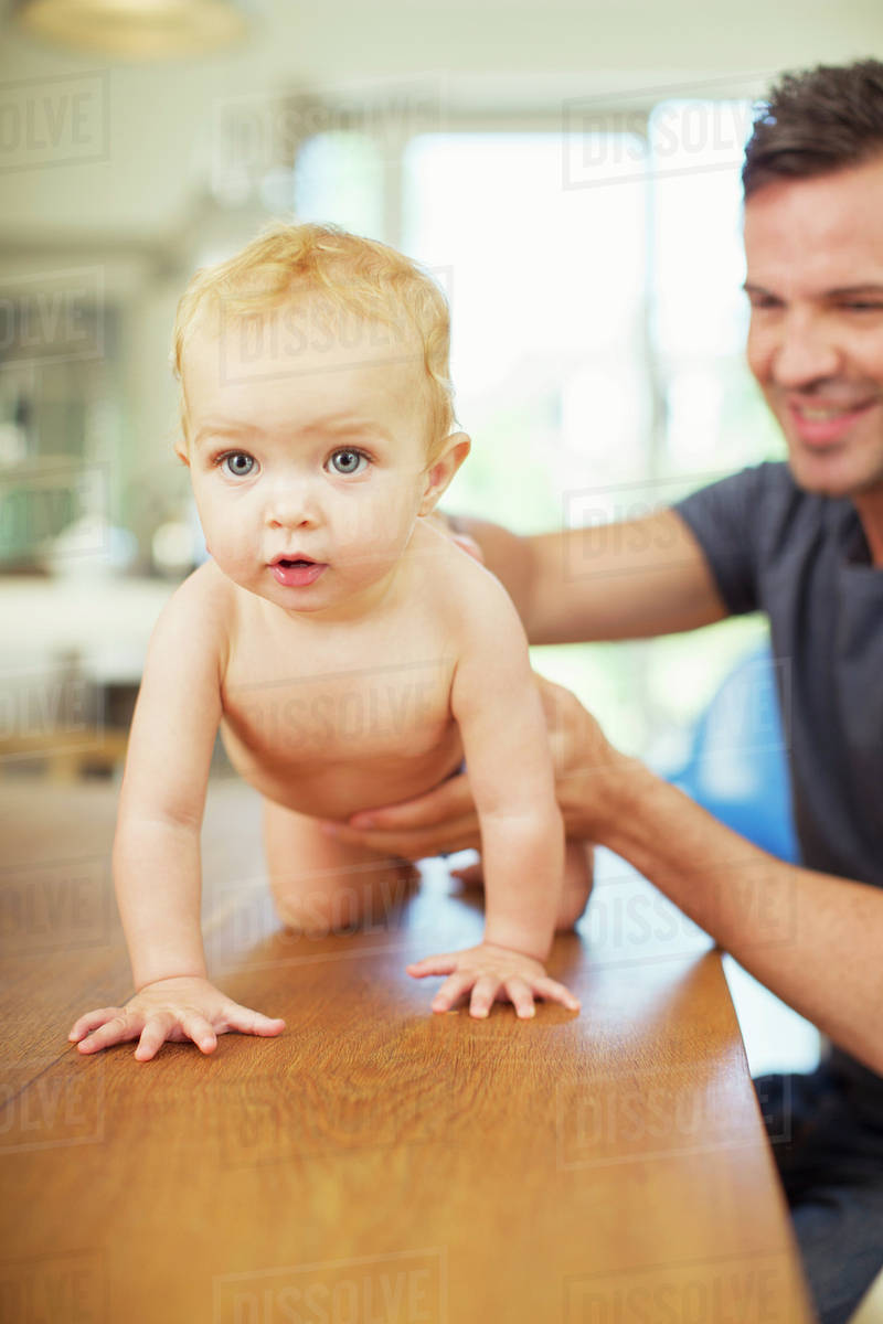 Father helping baby crawl on table - Stock Photo - Dissolve