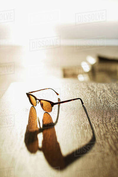 Sunglasses casting shadow on table - Stock Photo - Dissolve