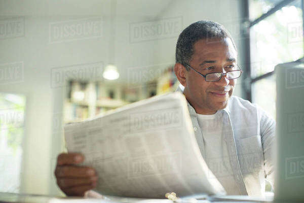 Senior man with newspaper using laptop - Royalty-free Stock Photo ...