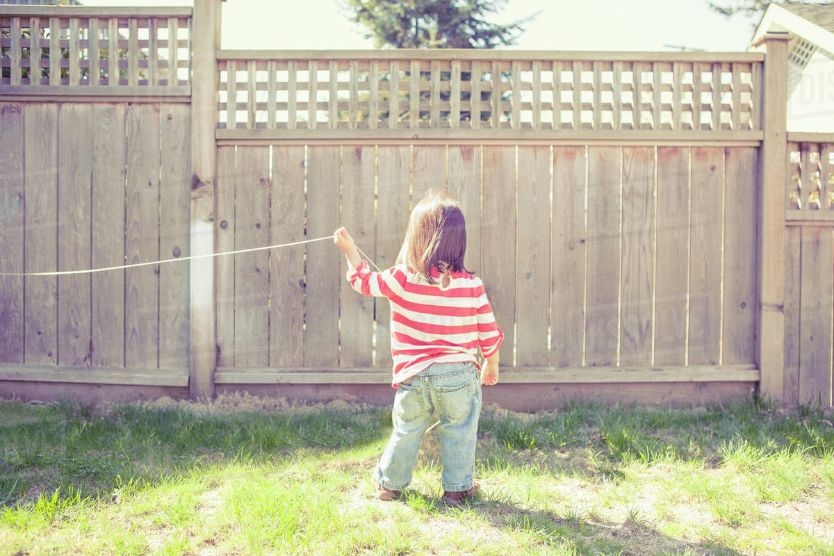 Baby girl playing with string in backyard - Stock Photo - Dissolve