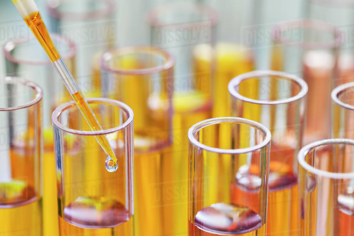 Close up of pipette dropping solution into test tube in rack in lab ...