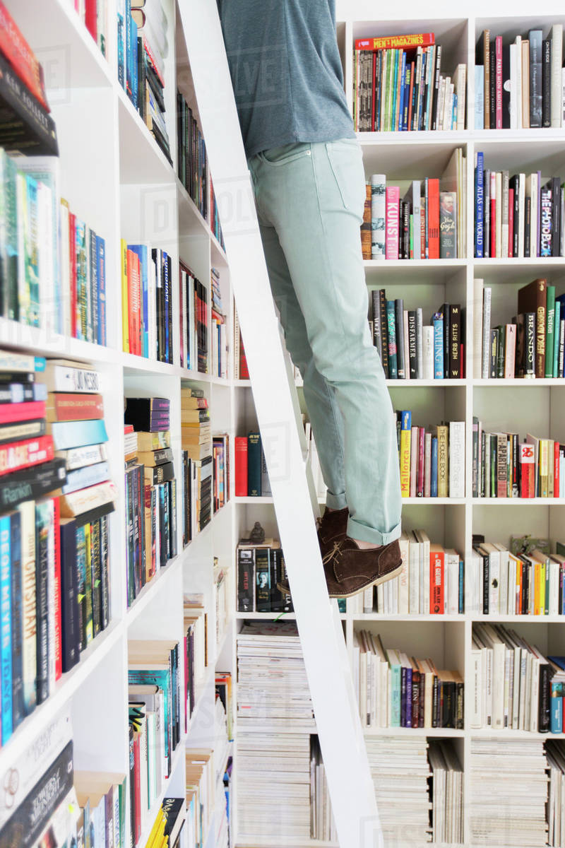 Man standing on ladder to reach books in library - Royalty-free Stock ...