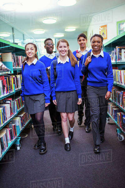 Students wearing school uniforms walking between bookshelves in library ...