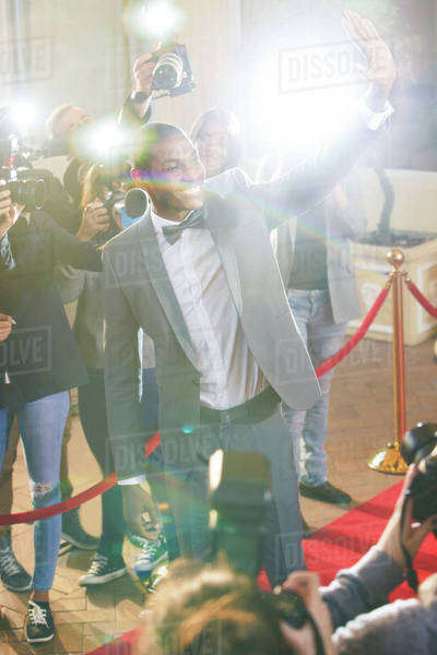 Smiling celebrity waving and being photographed by paparazzi ...