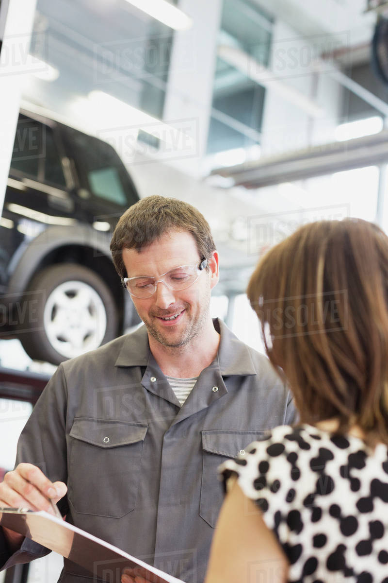 Mechanic with clipboard talking to customer in auto repair shop ...