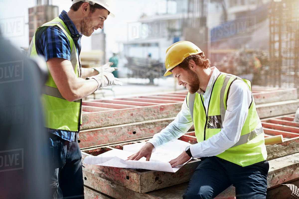 Construction worker and engineer reviewing blueprints at construction ...