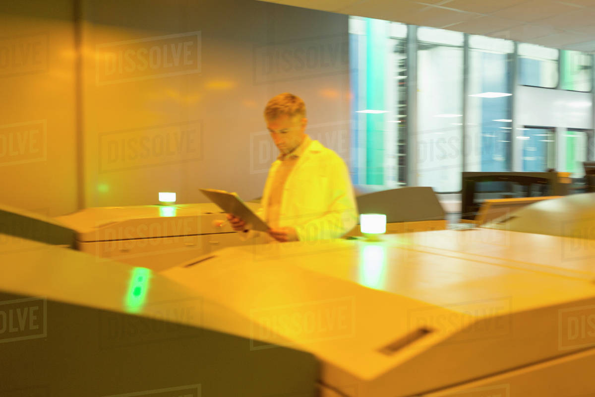 Worker with clipboard walking along printers in printing plant - Stock ...