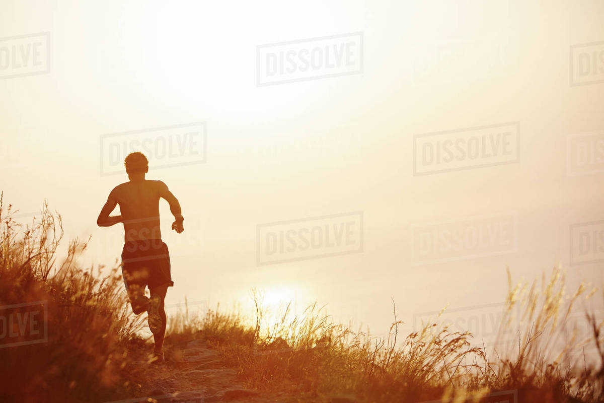 Man running on trail overlooking sunset ocean - Stock Photo - Dissolve