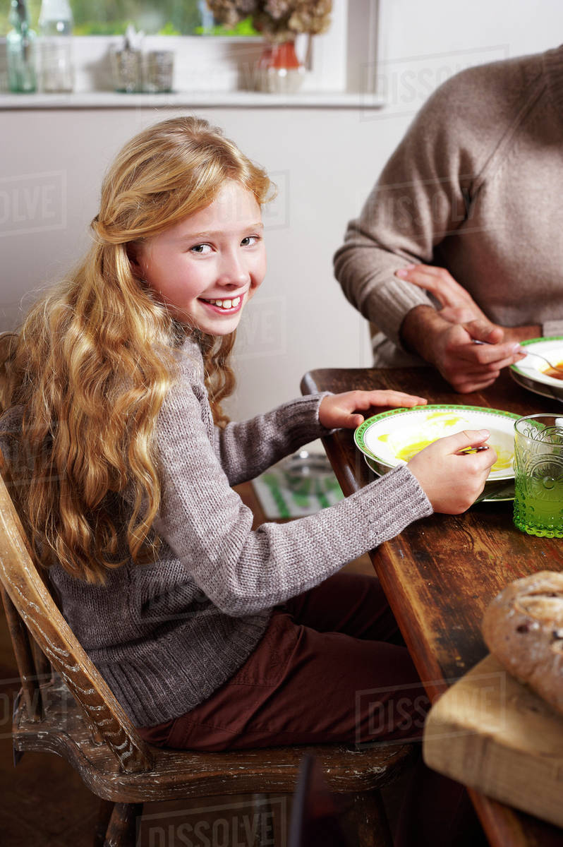Smiling girl eating at table - Royalty-free Stock Photo | Dissolve