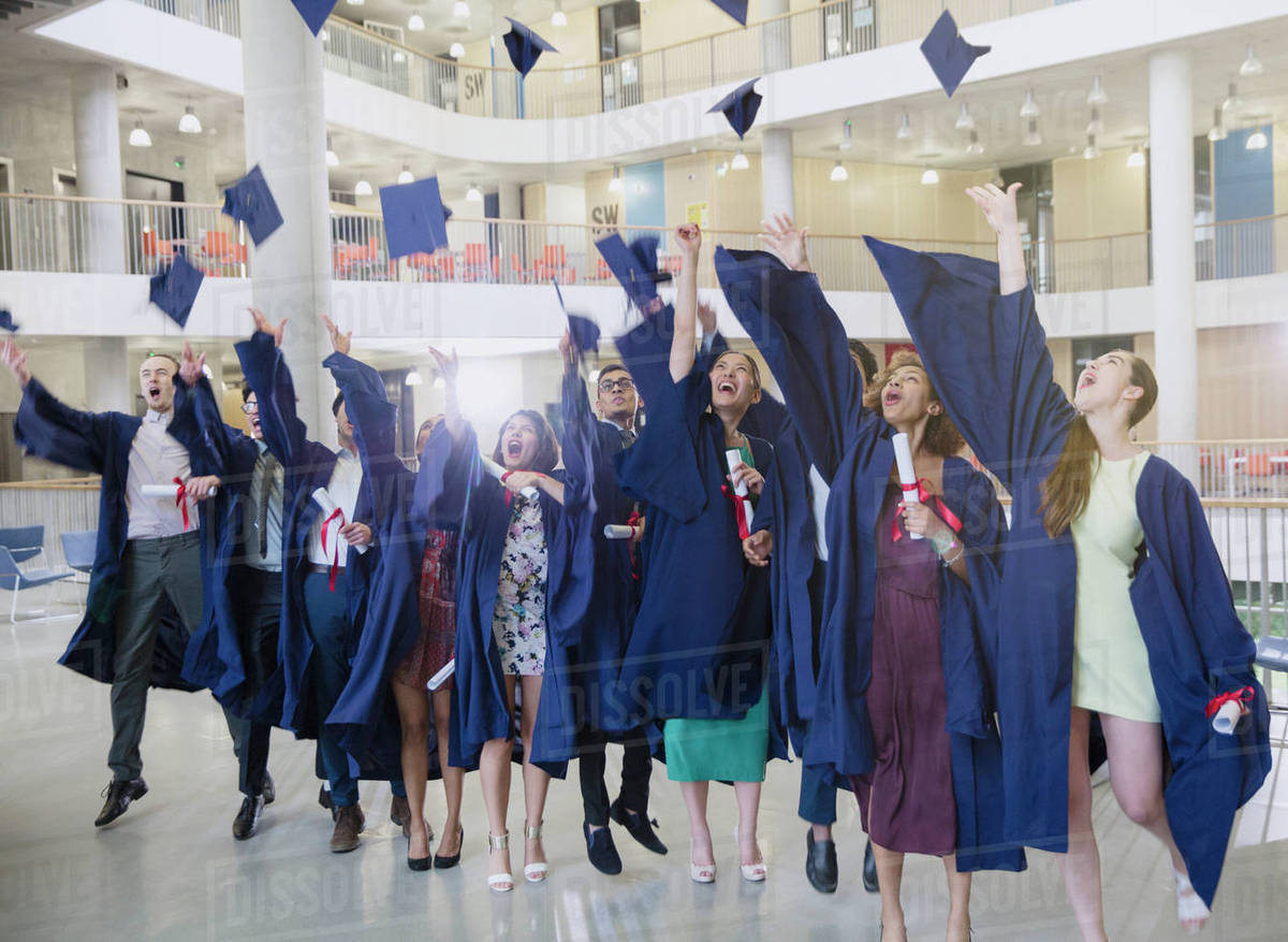 College graduates in cap and gown throwing caps overhead - Royalty-free ...