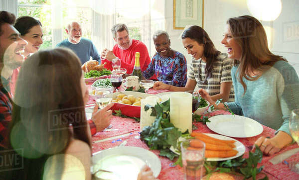 Laughing multi-ethnic family enjoying Christmas dinner at table ...