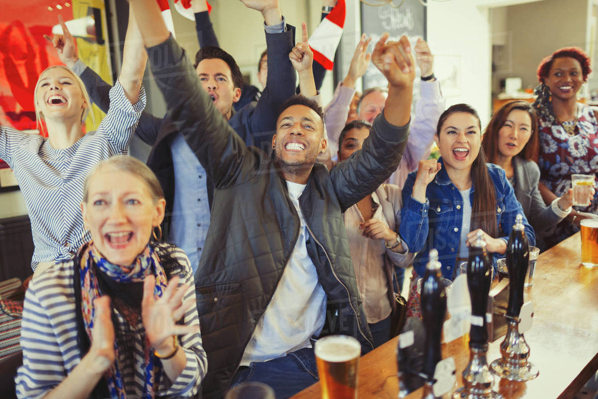 Enthusiastic sports fans cheering and watching game at bar - Royalty ...