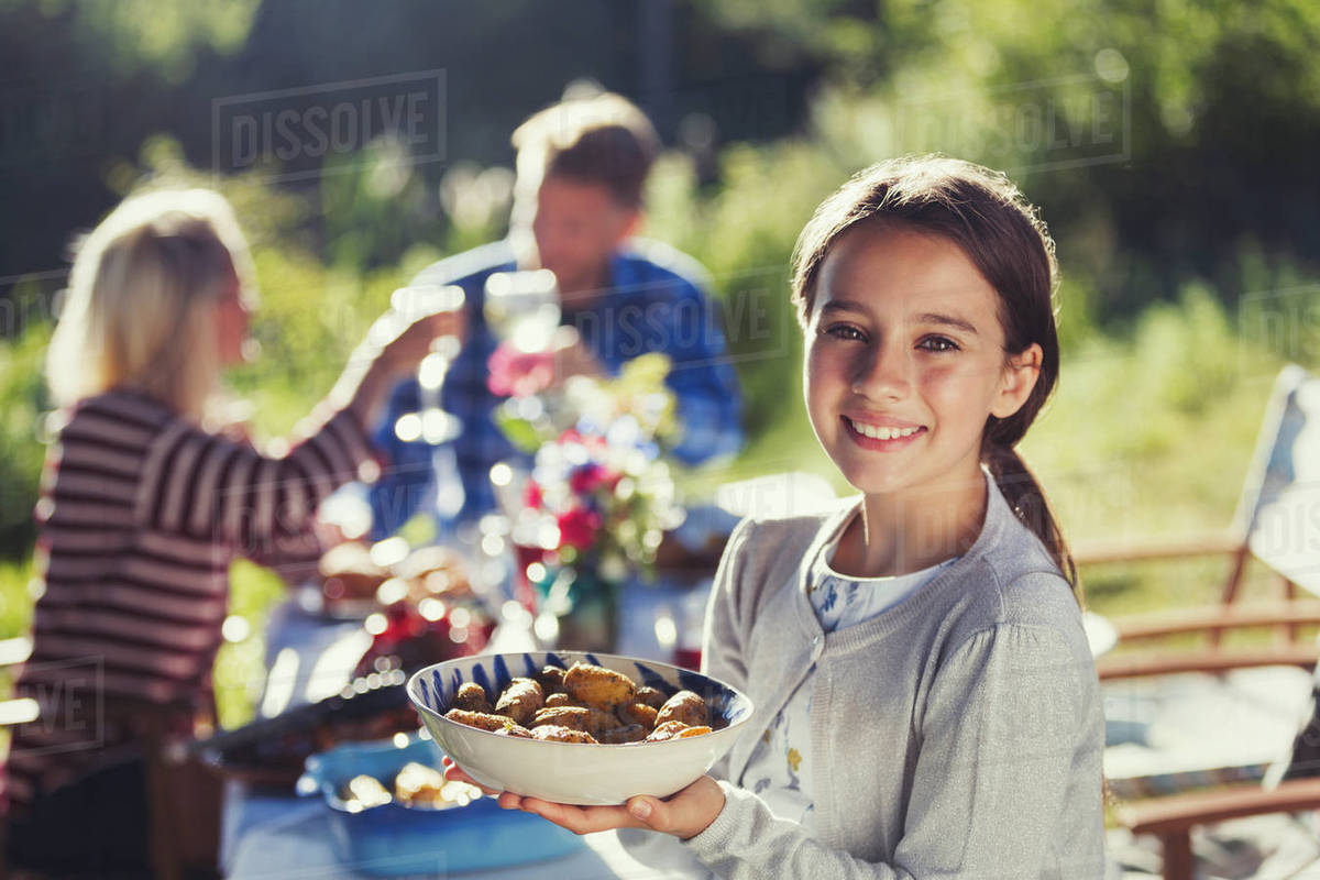Portrait smiling girl serving food at sunny garden party patio table ...