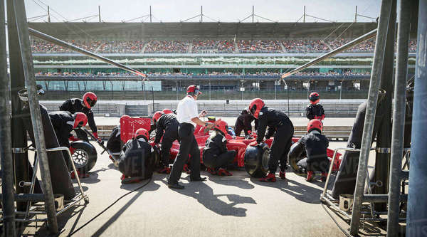 Manager and pit crew replacing tires on formula one race car in pit ...