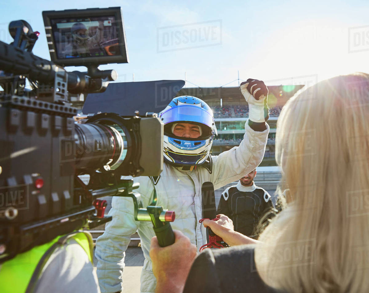 News reporter and cameraman interviewing formula one driver cheering ...