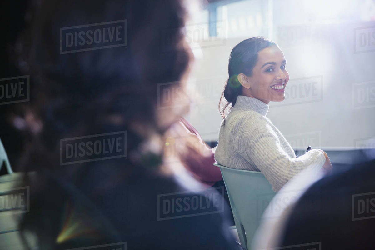Smiling businesswoman turning, looking back in conference audience ...