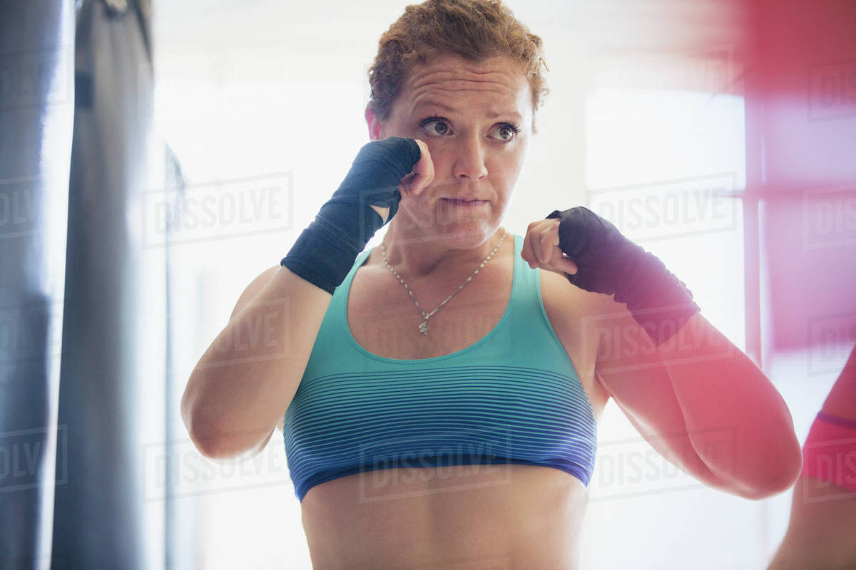 Determined female boxer with wrist wraps in fighting stance at gym ...