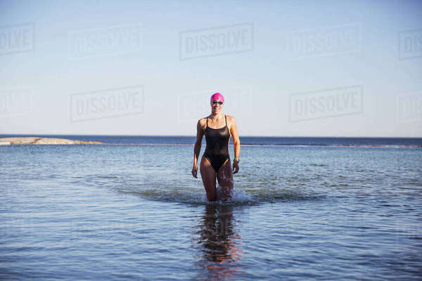 Portrait female open water swimmer wading, walking in sunny ocean surf ...