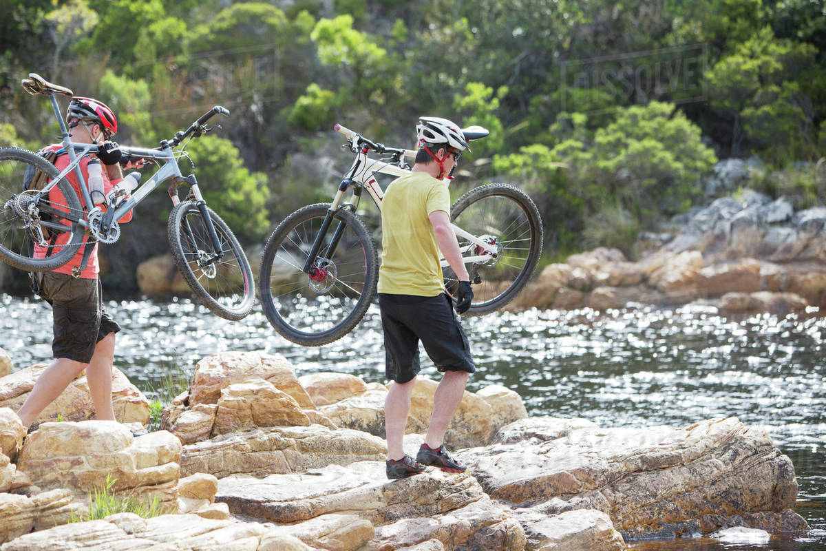 Men carrying mountain bikes on rock formation - Stock Photo - Dissolve