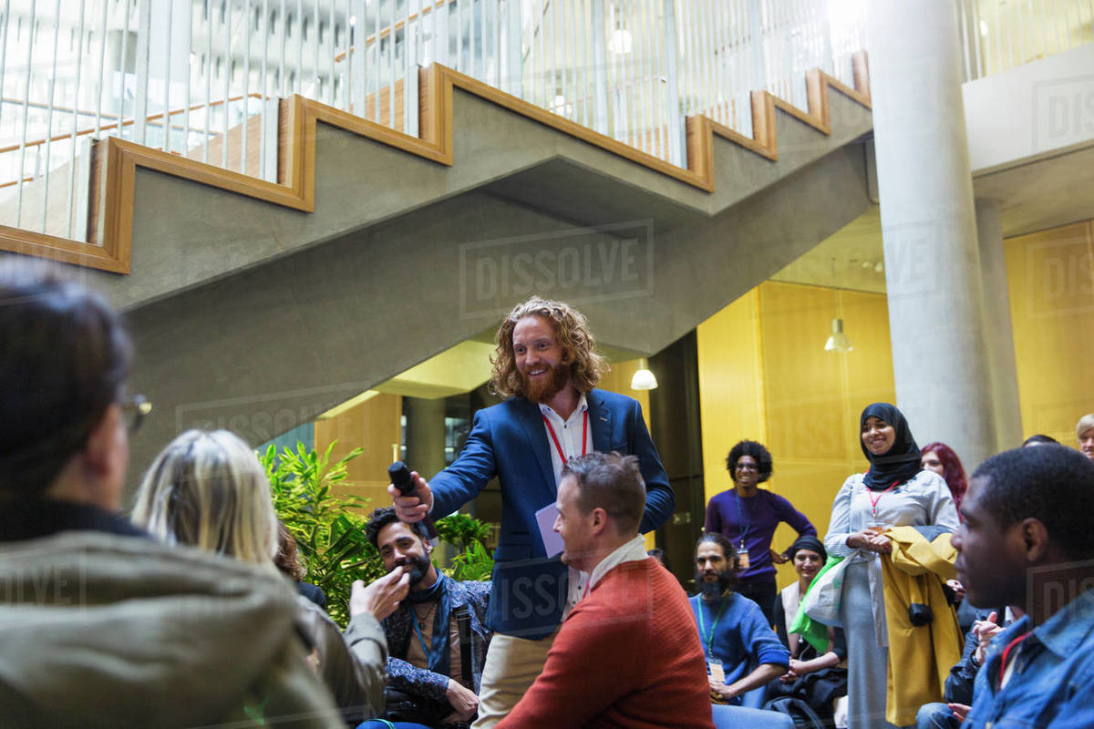 Smiling male speaker giving microphone to woman in audience - Stock ...