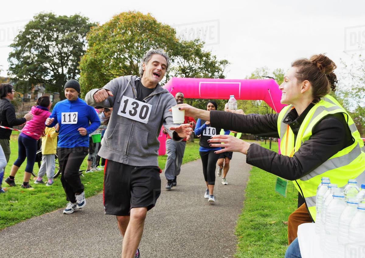 Volunteer giving water to runner at charity run in park - Stock Photo ...