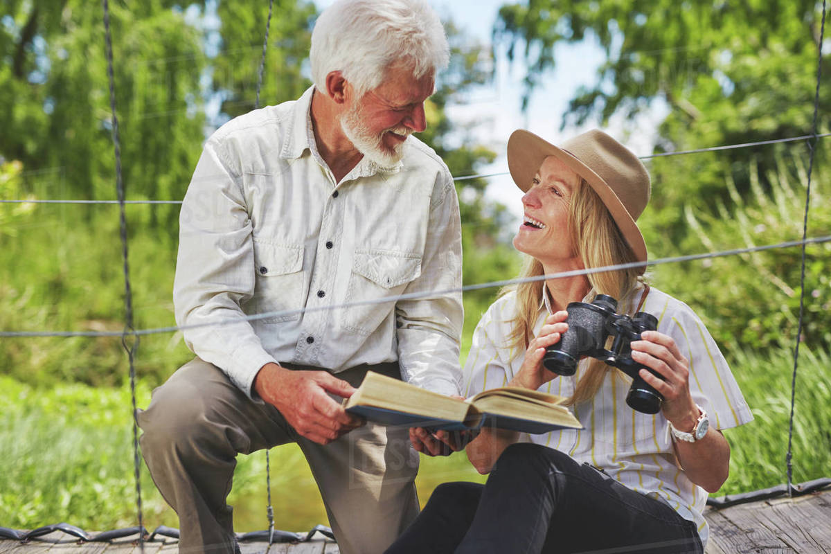 Smiling active senior couple bird watching with binoculars and book ...