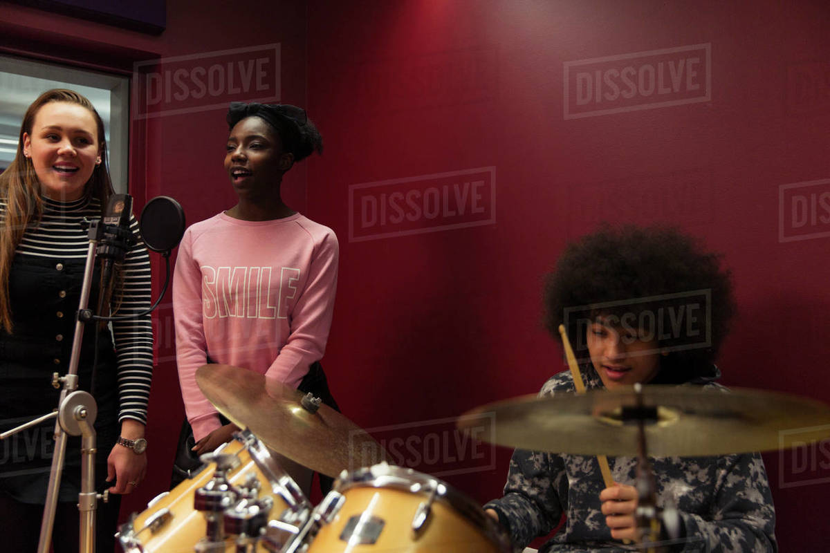 Teenage musicians recording music, singing and playing drums in sound ...
