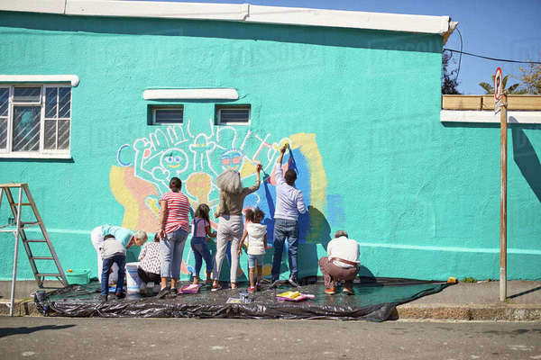 Community volunteers painting vibrant mural on sunny urban wall - Stock ...