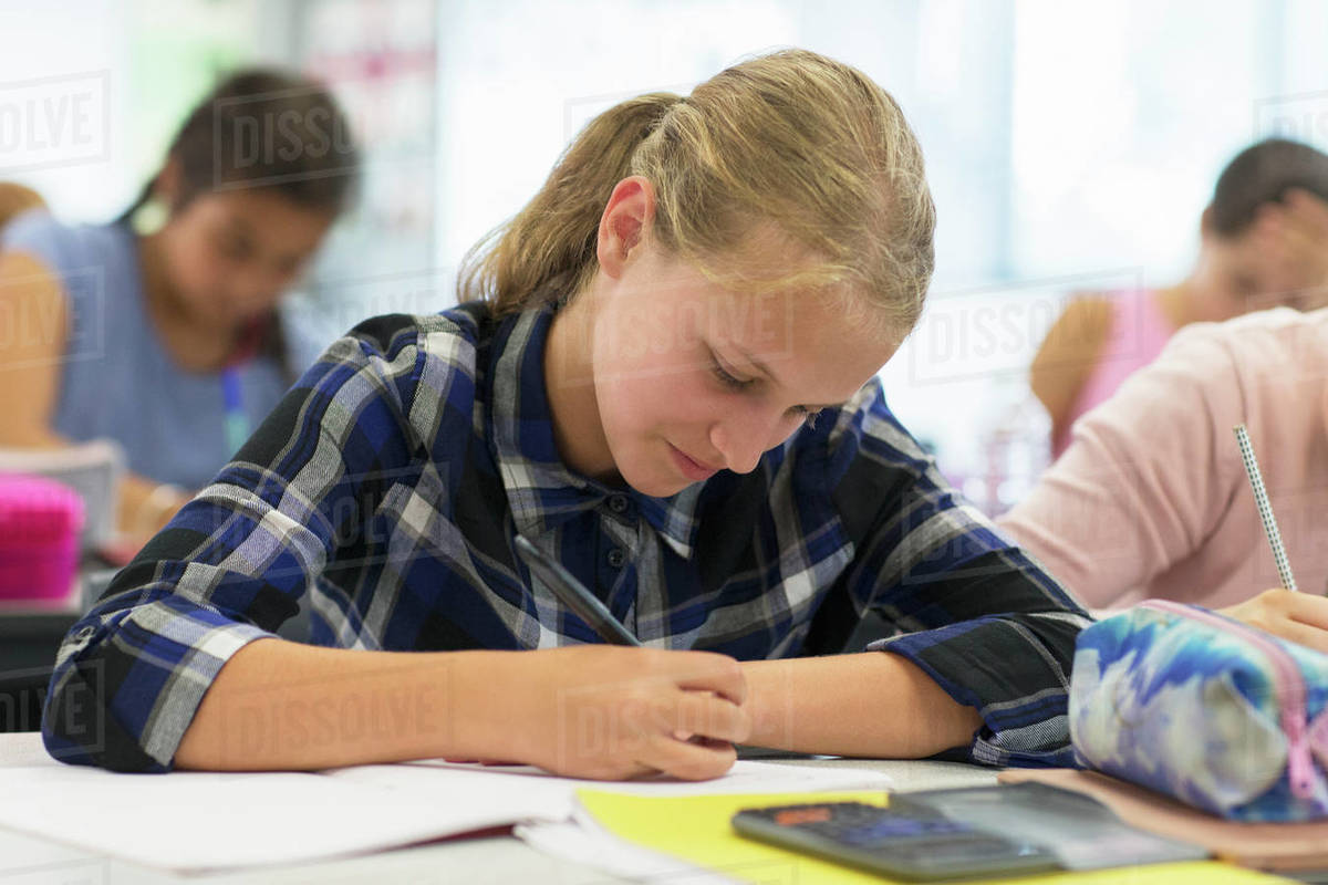 Focused junior high school student doing homework in classroom ...