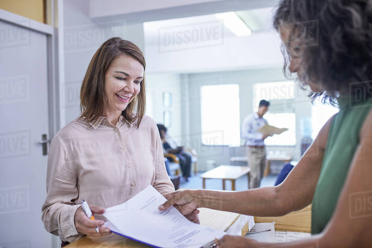 Receptionist helping woman with paperwork at clinic reception - Stock ...