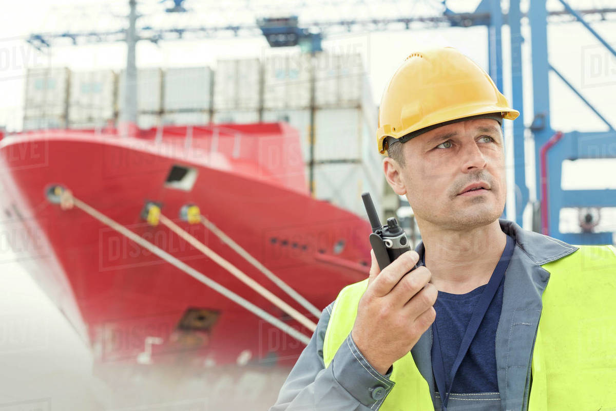 Dock worker using walkie-talkie below container ship at shipyard ...